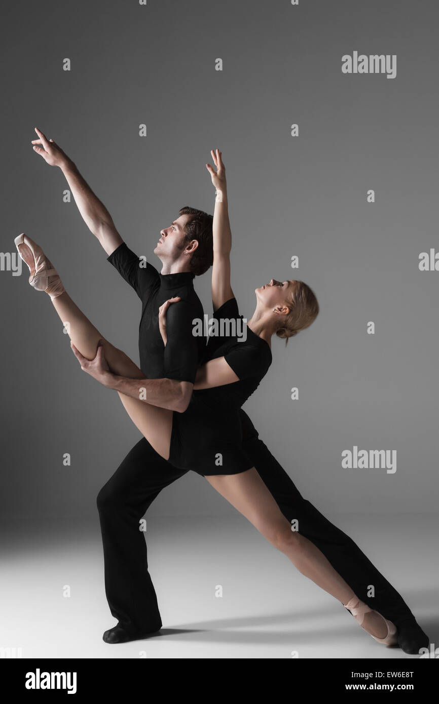 The two young modern ballet dancers in black suits posing over gray ...