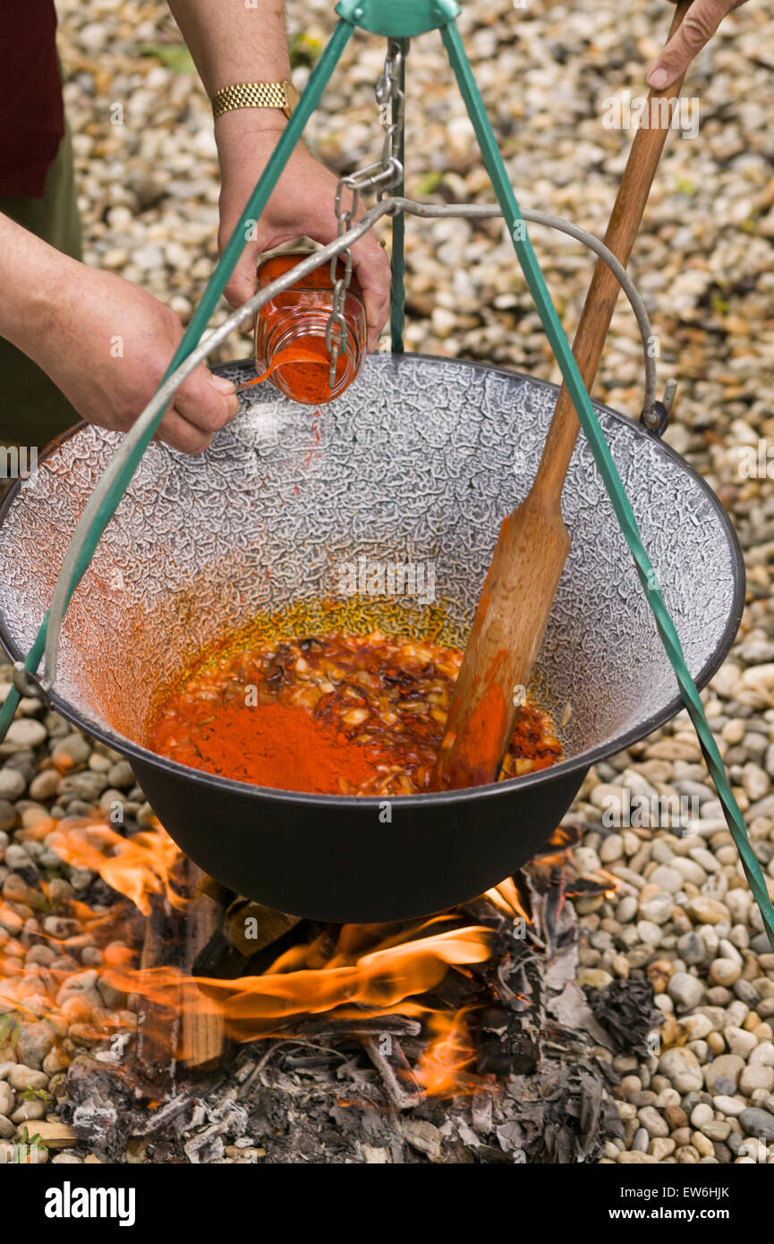 A person adds Paprika to Hungarian Goulash being made over a fire, in ...