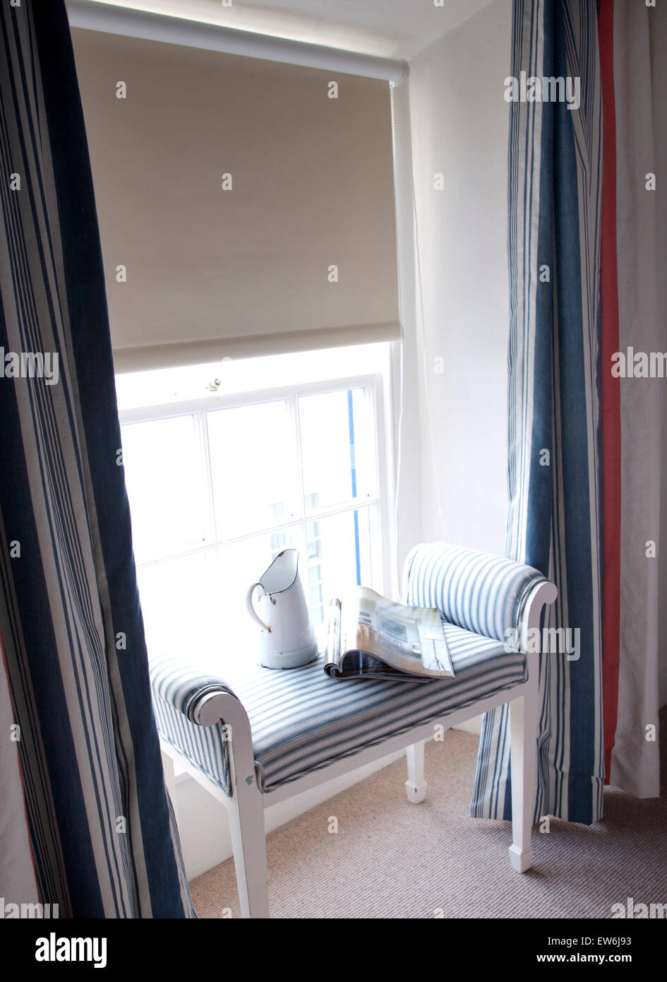 Blue striped upholstered stool in front of window with cream blind and ...
