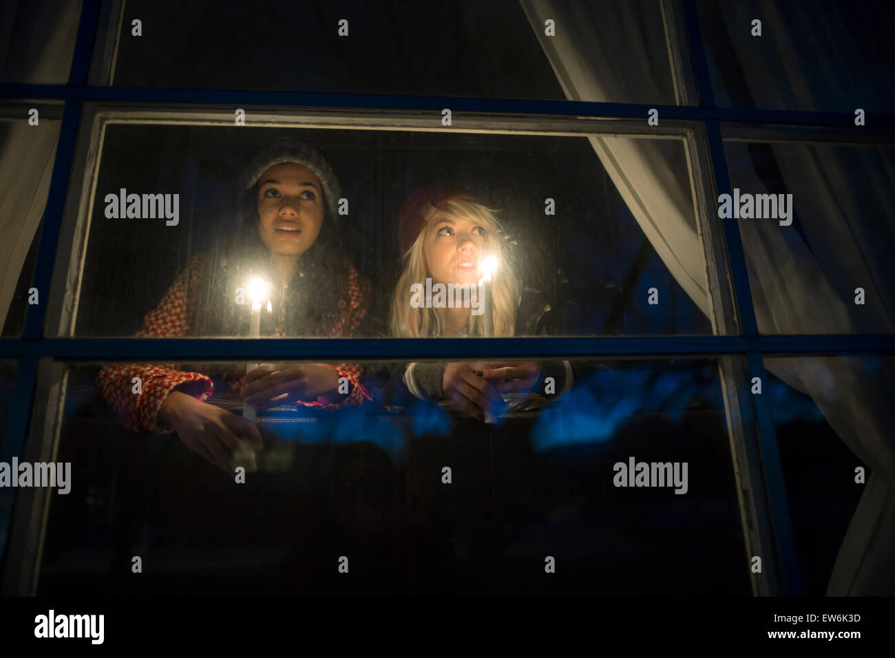 Two college girls peer out a dark window holding candles Stock Photo ...