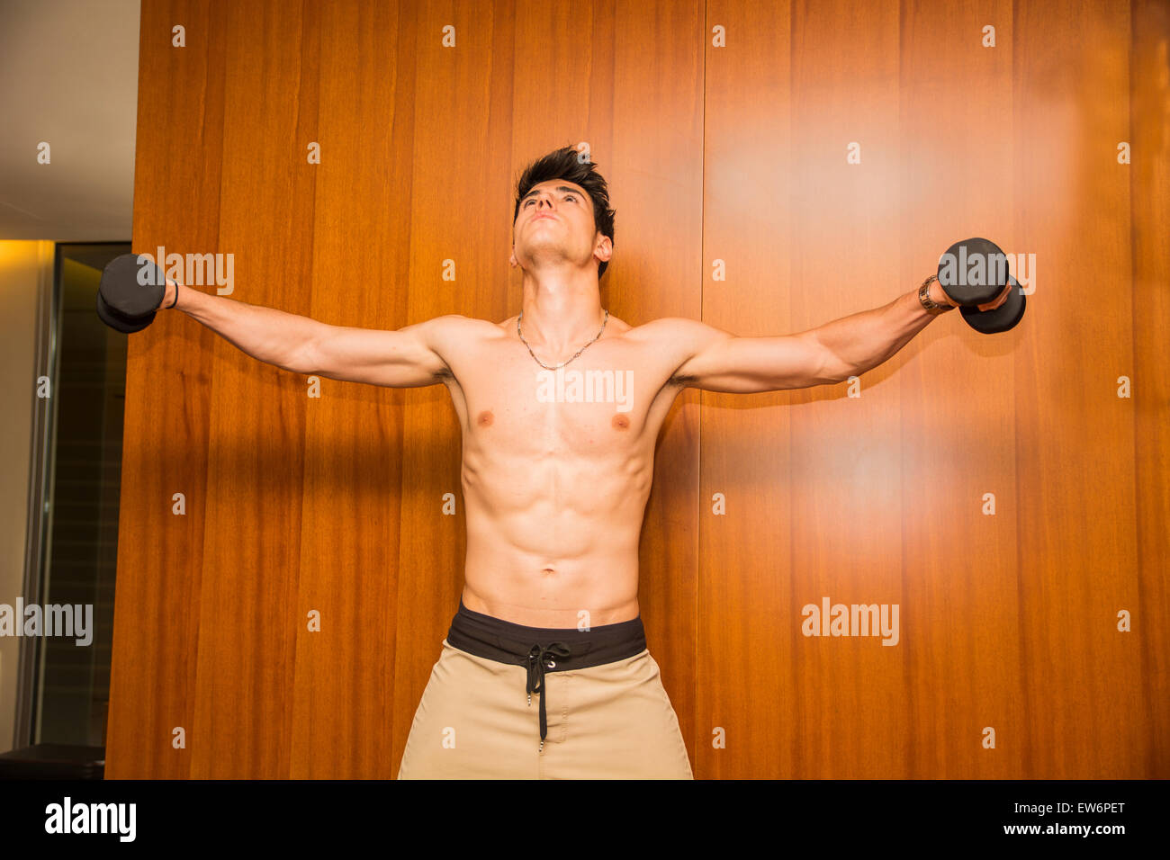 Handsome young man working out, exercising biceps with dumbbells at gym ...