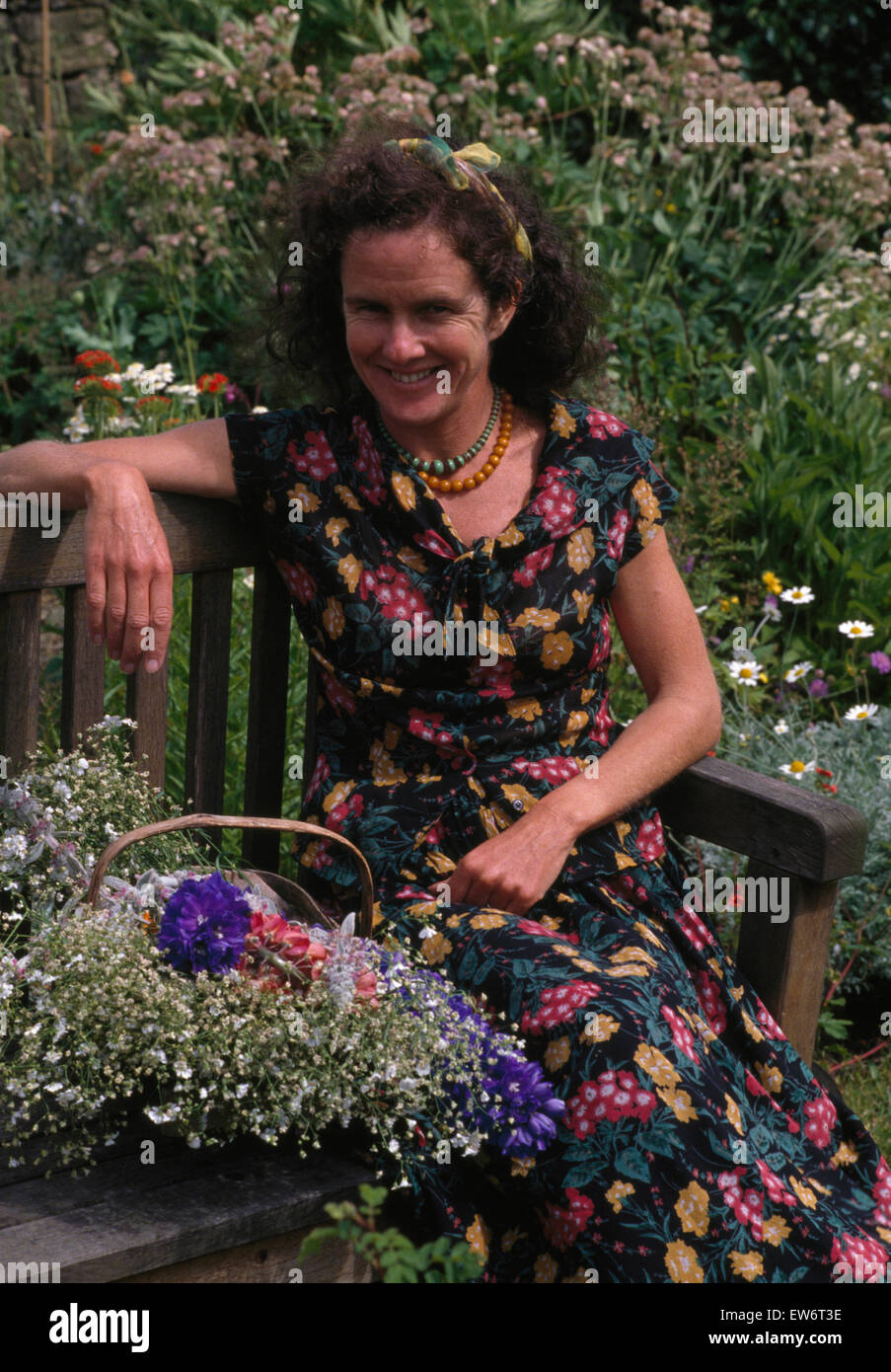 Portrait of a smiling woman sitting on a garden bench with a trug of ...