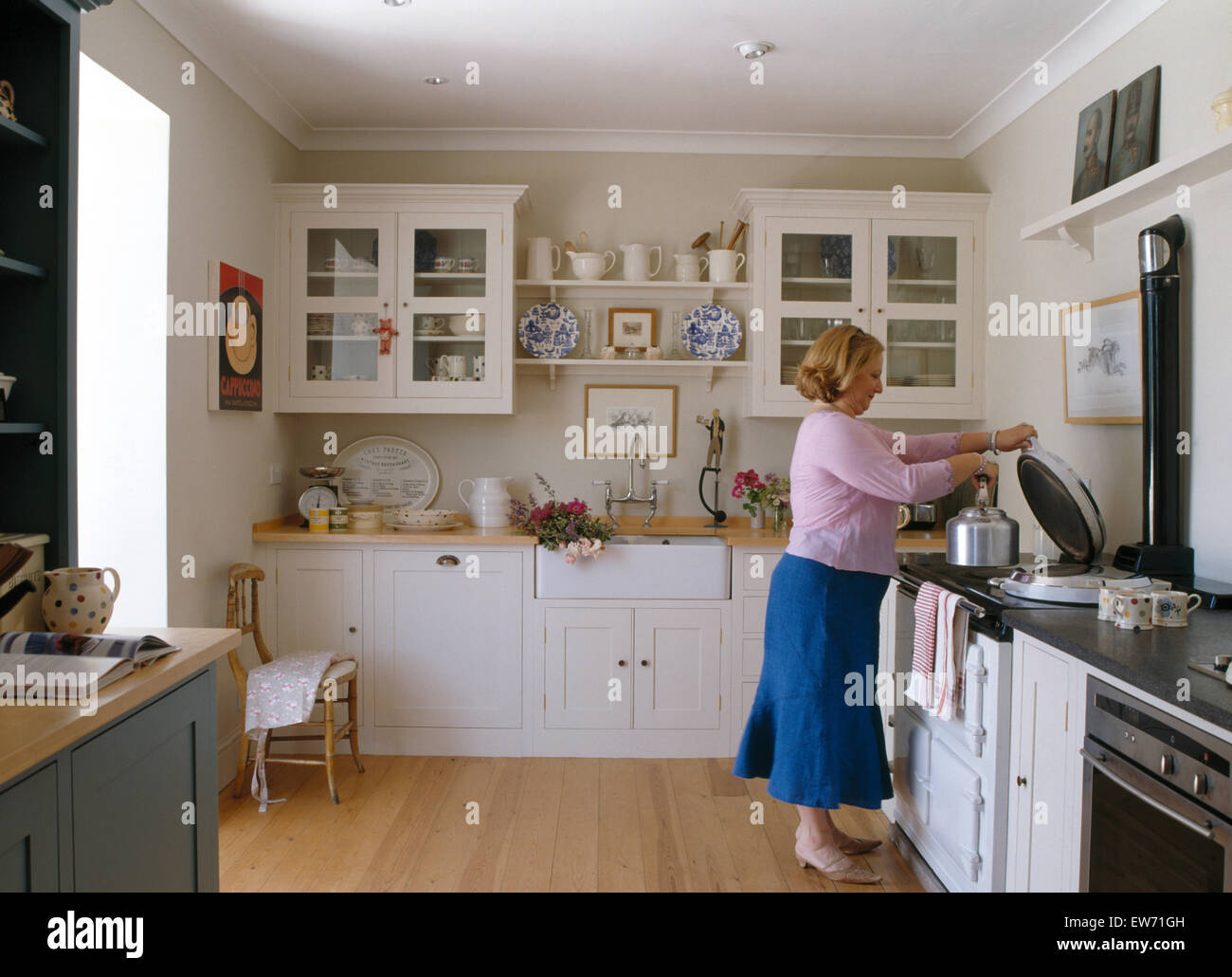 Woman standing and cooking on an Aga oven in a cottage kitchen FOR ...