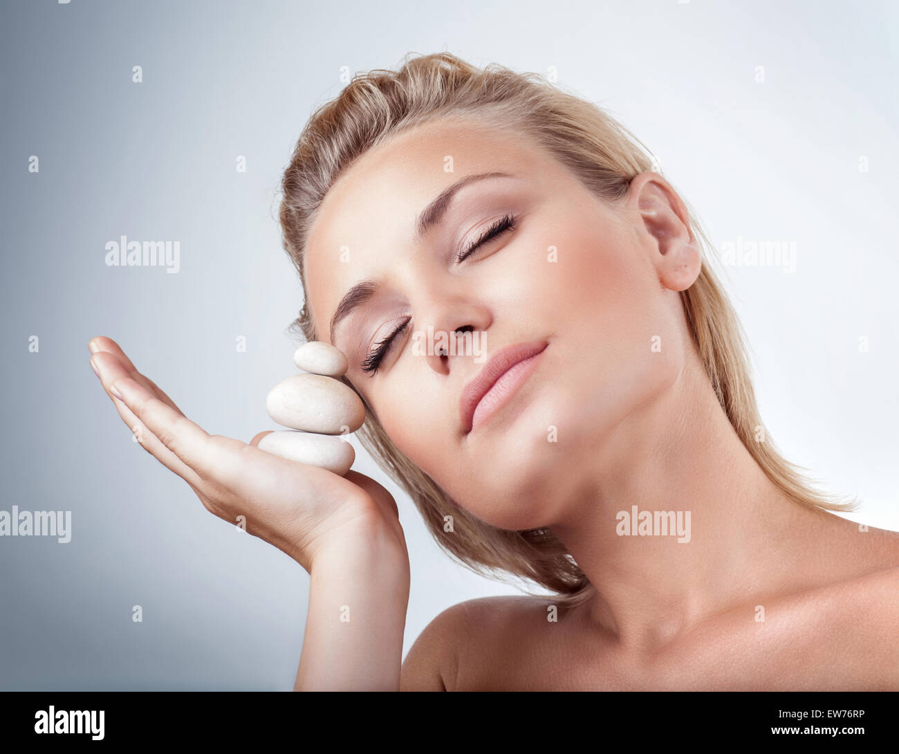 Portrait of gentle female with closed eyes holding on hand spa stones ...