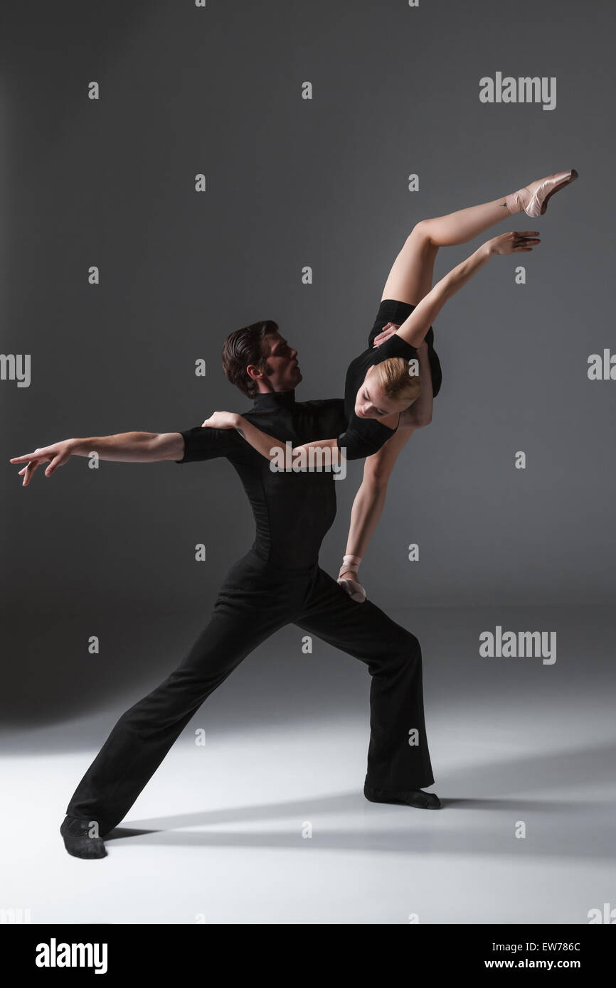 The two young modern ballet dancers in black suits posing over gray ...