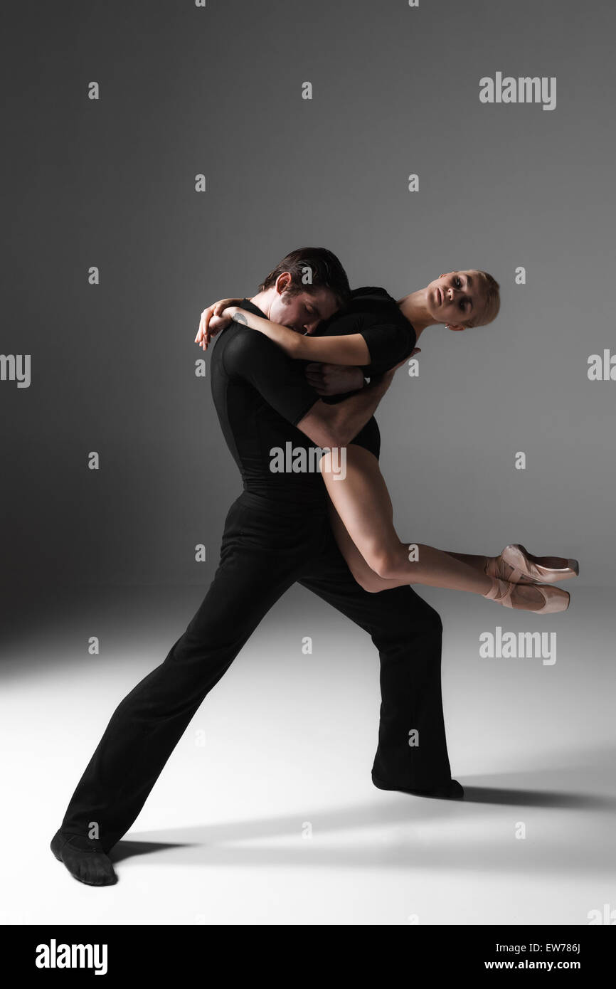 The two young modern ballet dancers in black suits posing over gray ...