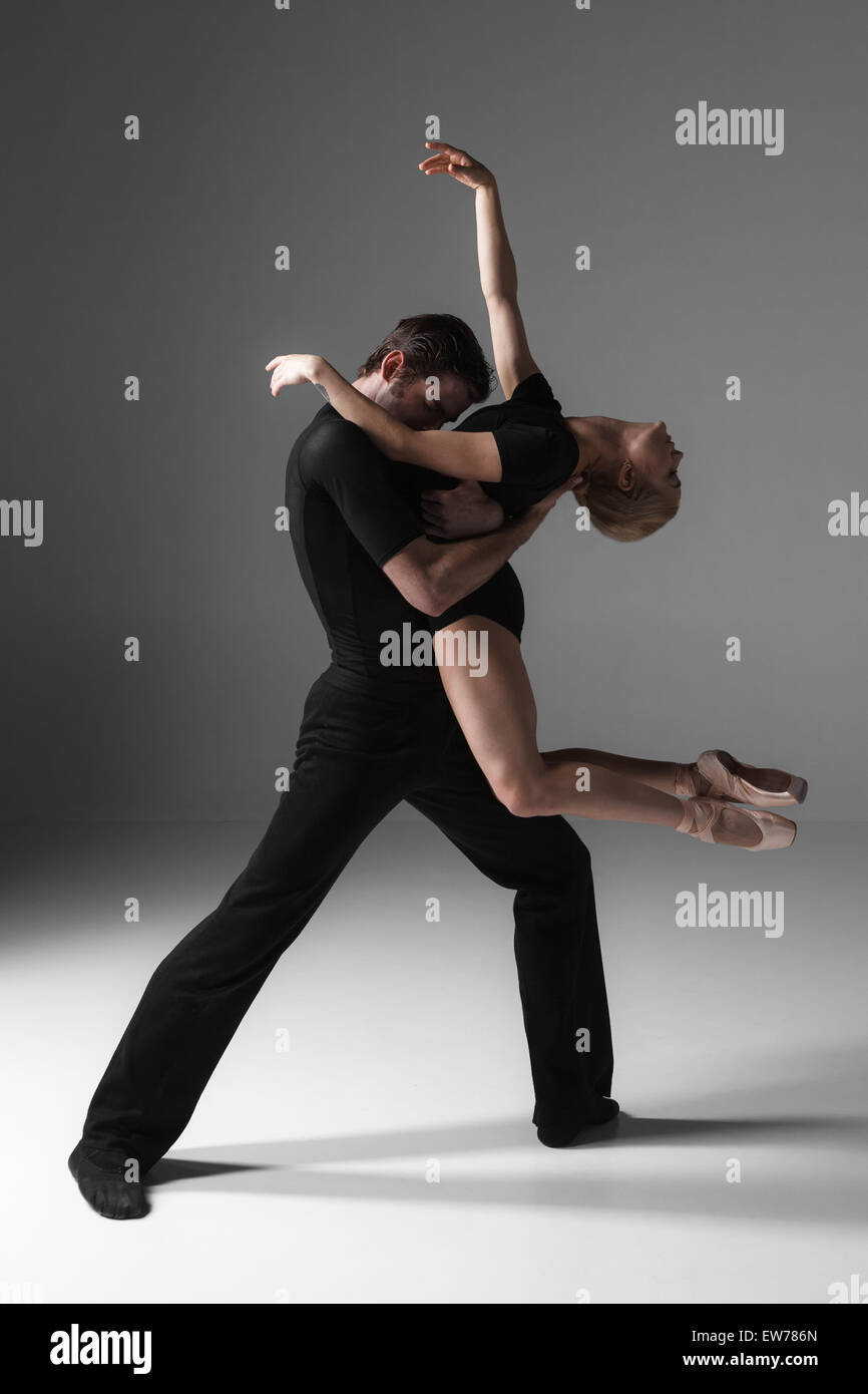 The two young modern ballet dancers in black suits posing over gray ...