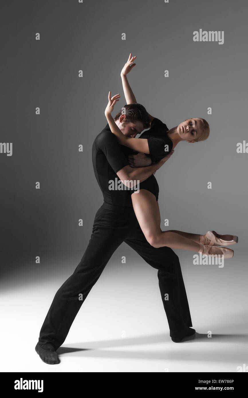 The two young modern ballet dancers in black suits posing over gray ...