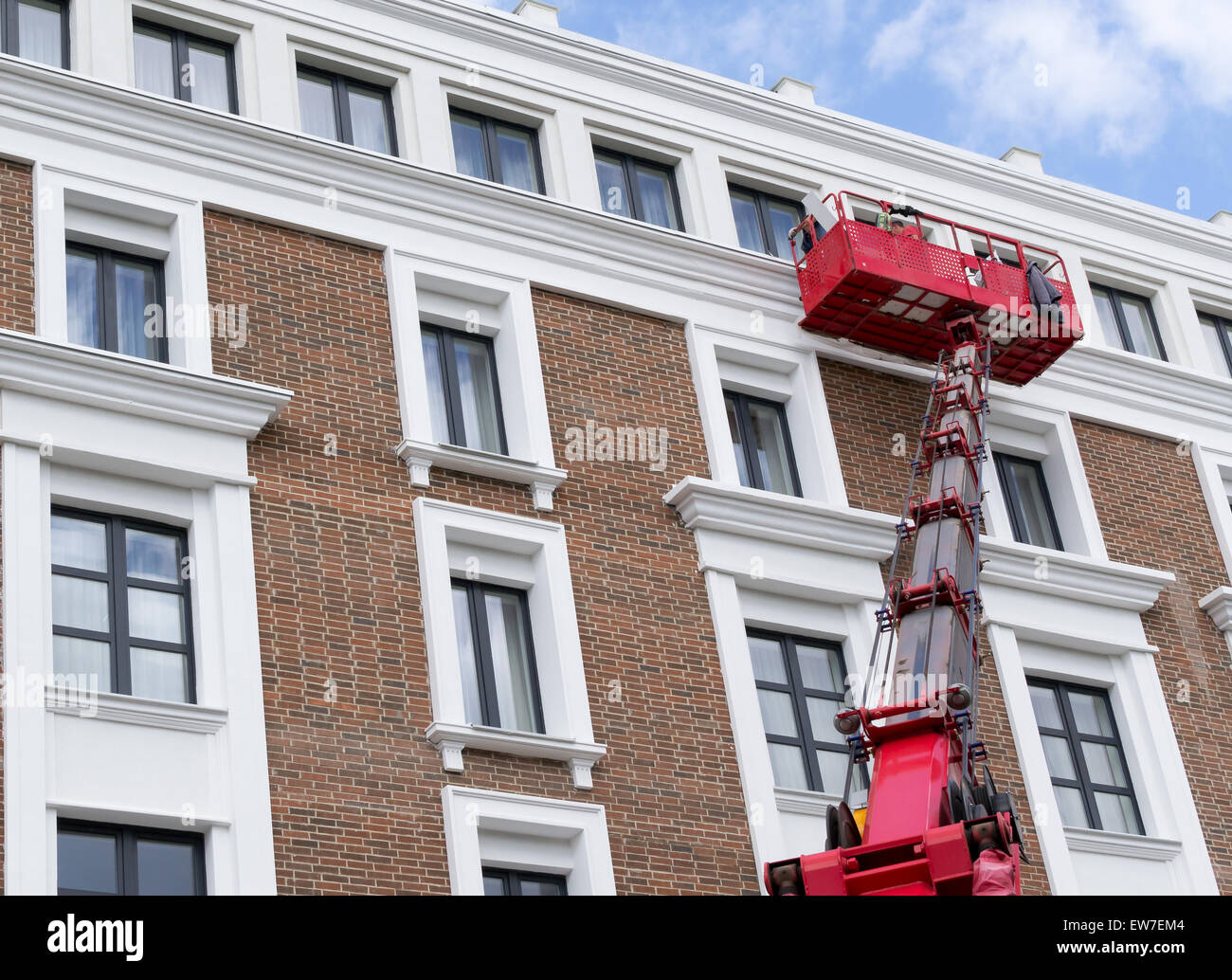 Workers working on a building facade using a red hydraulic lift Stock ...