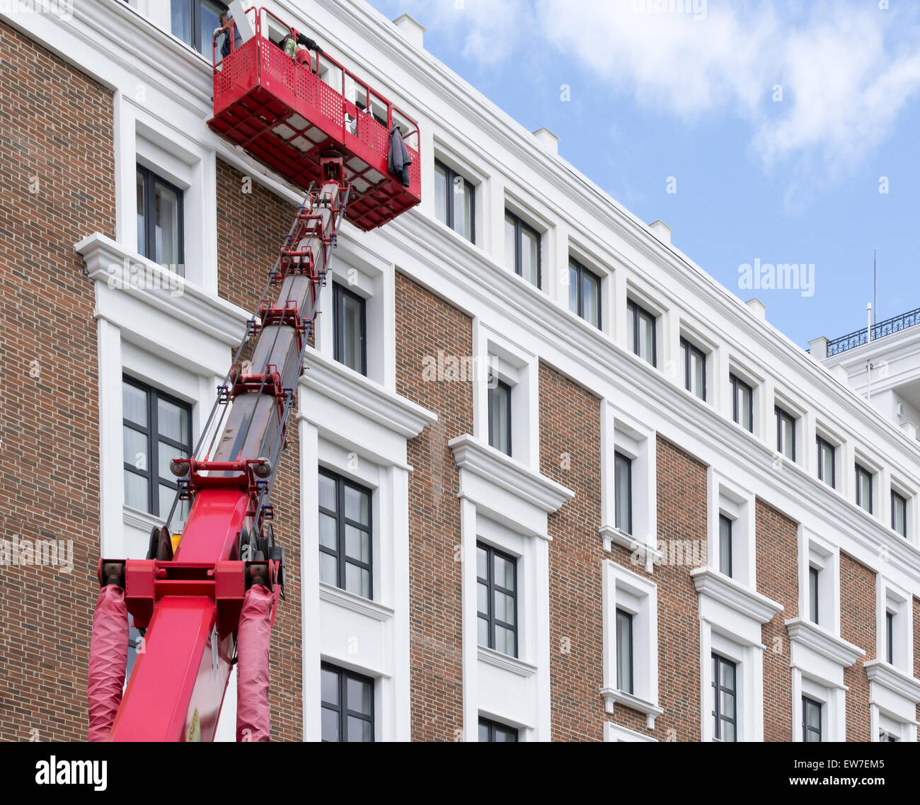 Workers working on a building facade using a red hydraulic lift Stock ...