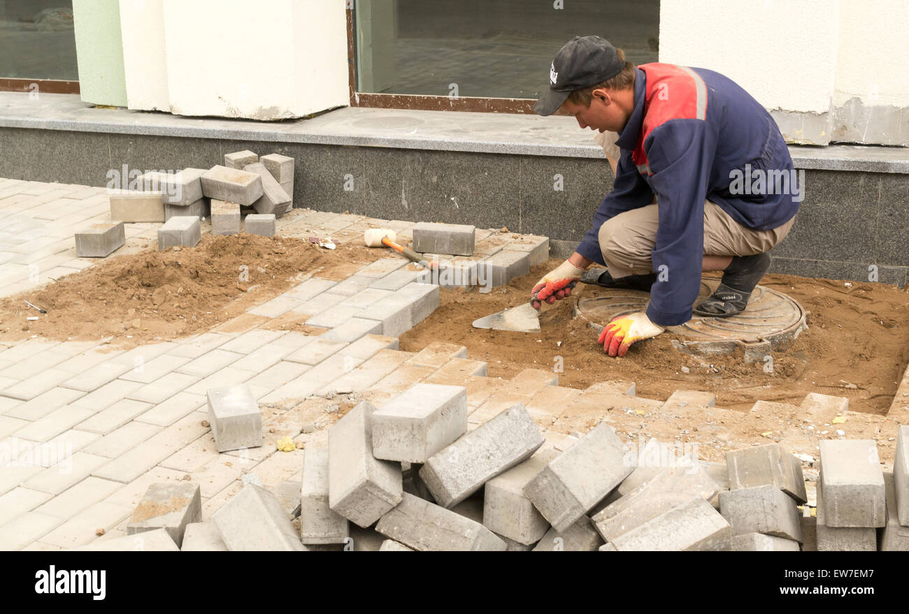 Uniformed builder lays sand foundation for stone brick block paving in ...