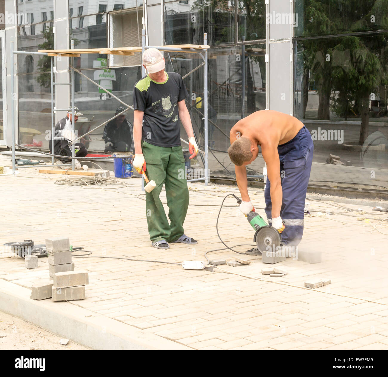 Two city workers using a grinding machine to cut brick blocks for a ...