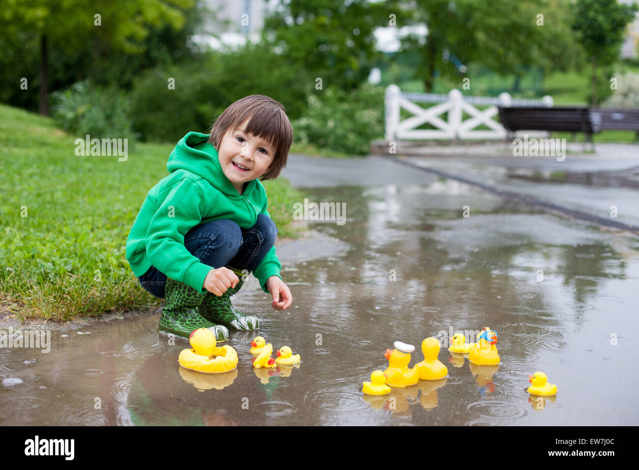 Little boy, jumping and playing in muddy puddles in the park, rubber ...