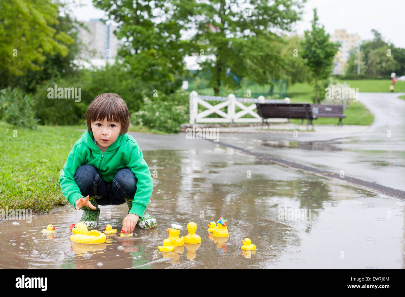 Little boy, jumping and playing in muddy puddles in the park, rubber ...