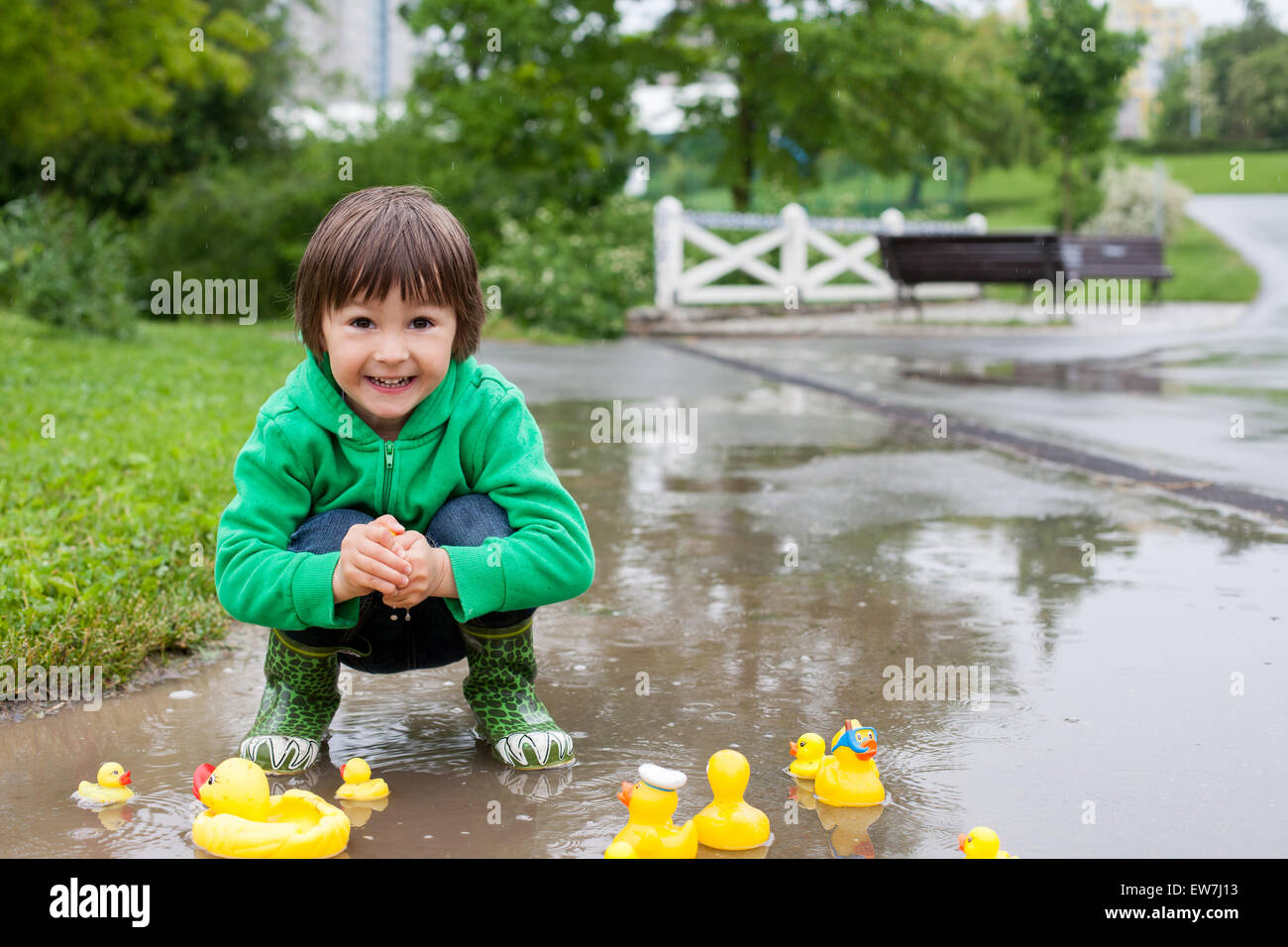 Little boy, jumping and playing in muddy puddles in the park, rubber ...