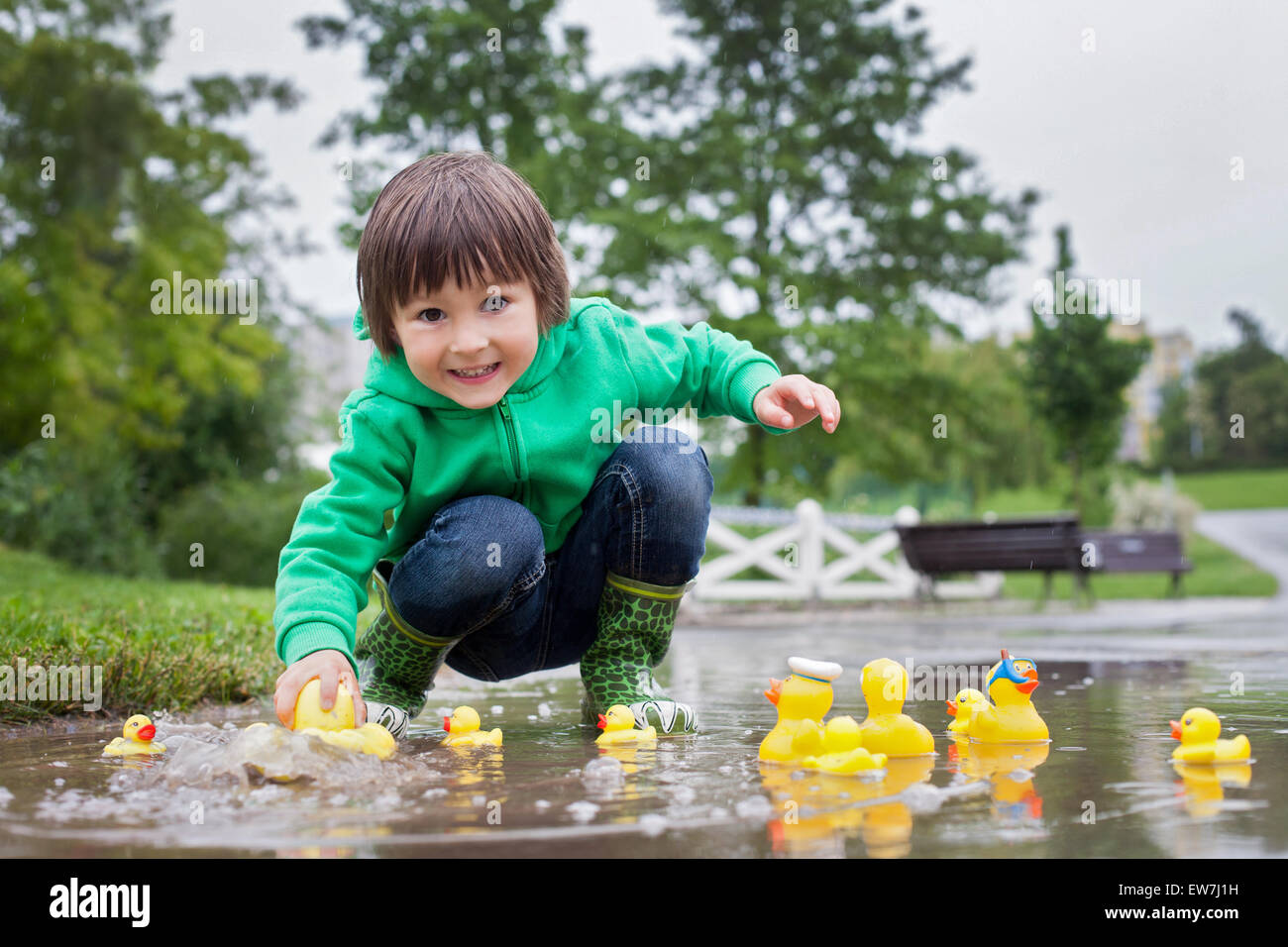 Little boy, jumping and playing in muddy puddles in the park, rubber ...