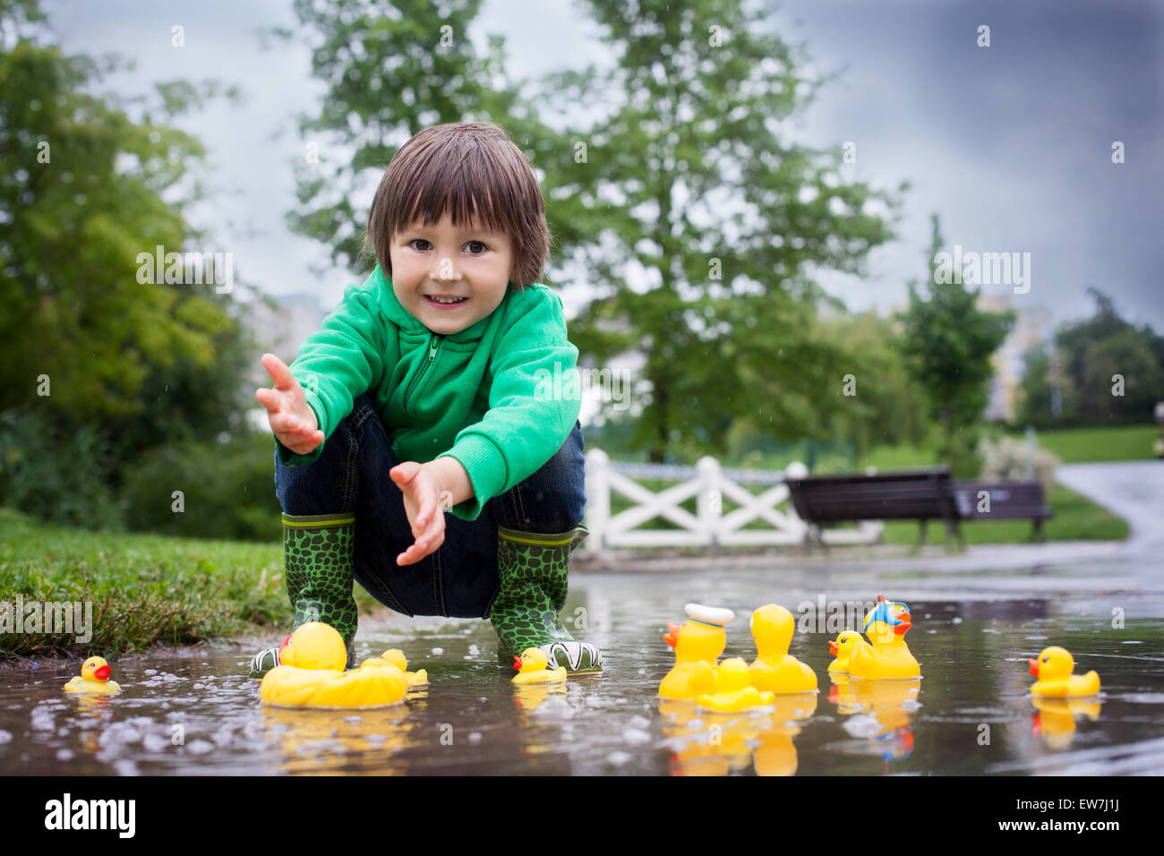 Little boy, jumping and playing in muddy puddles in the park, rubber ...