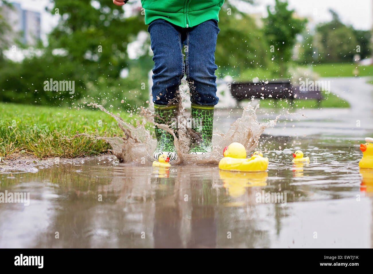 Little boy, jumping and playing in muddy puddles in the park, rubber ...