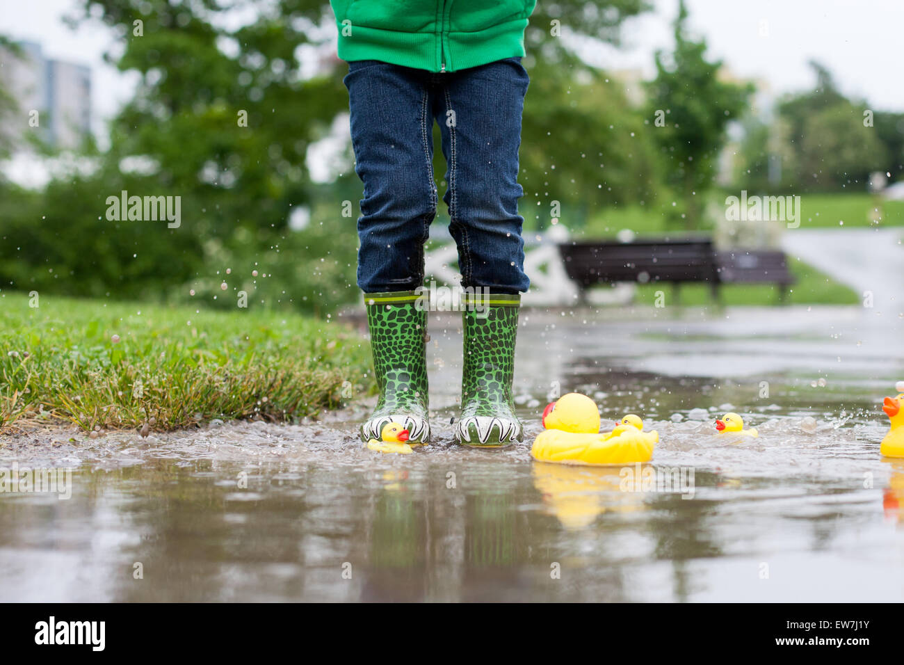 Little boy, jumping and playing in muddy puddles in the park, rubber ...