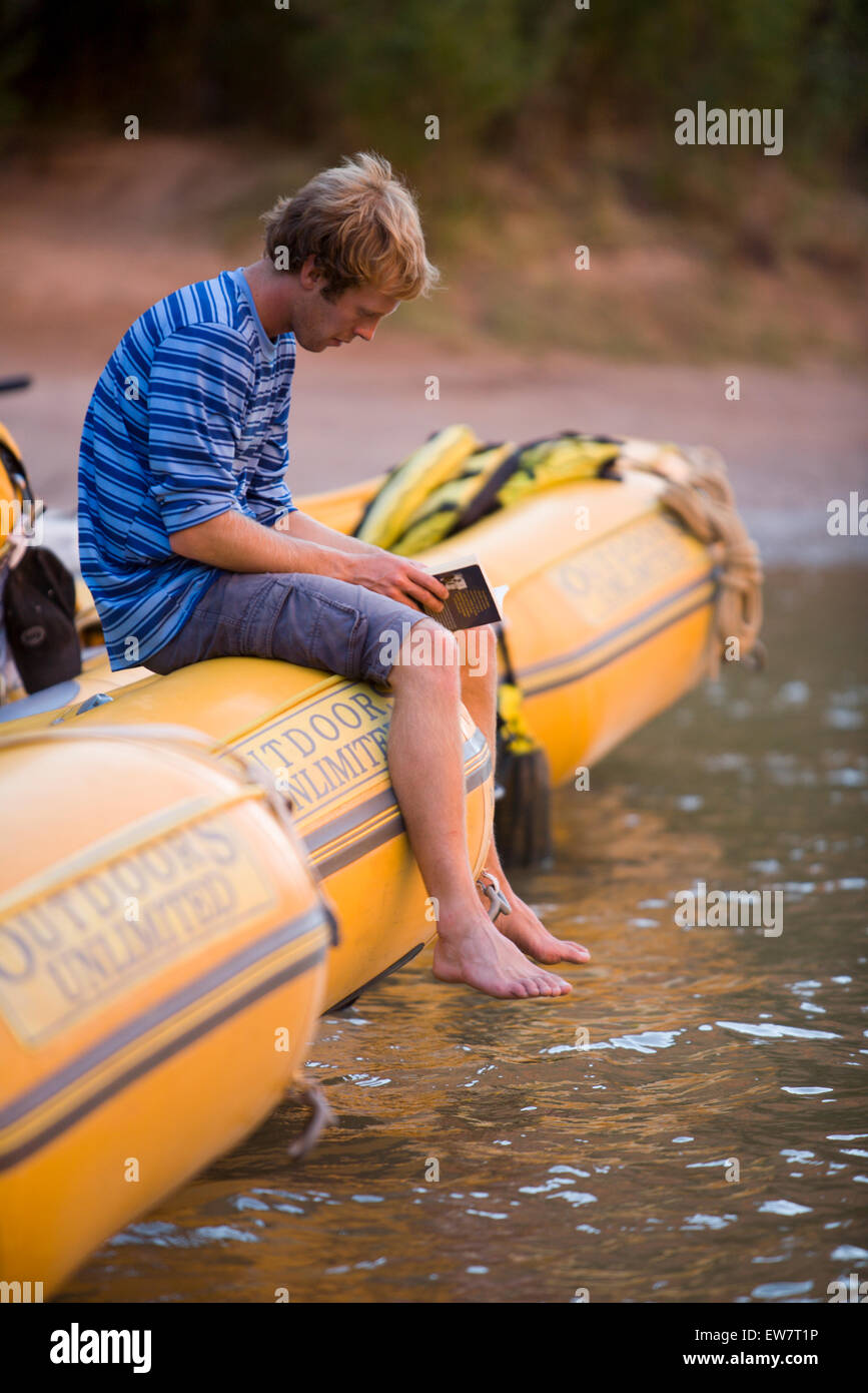 Man reading a book in a raft at the river's edge deep in a canyon Stock ...