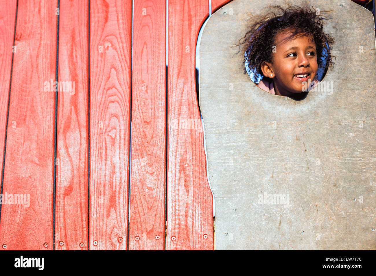 Smiling girl poking her head through hole in the wall hi-res stock ...