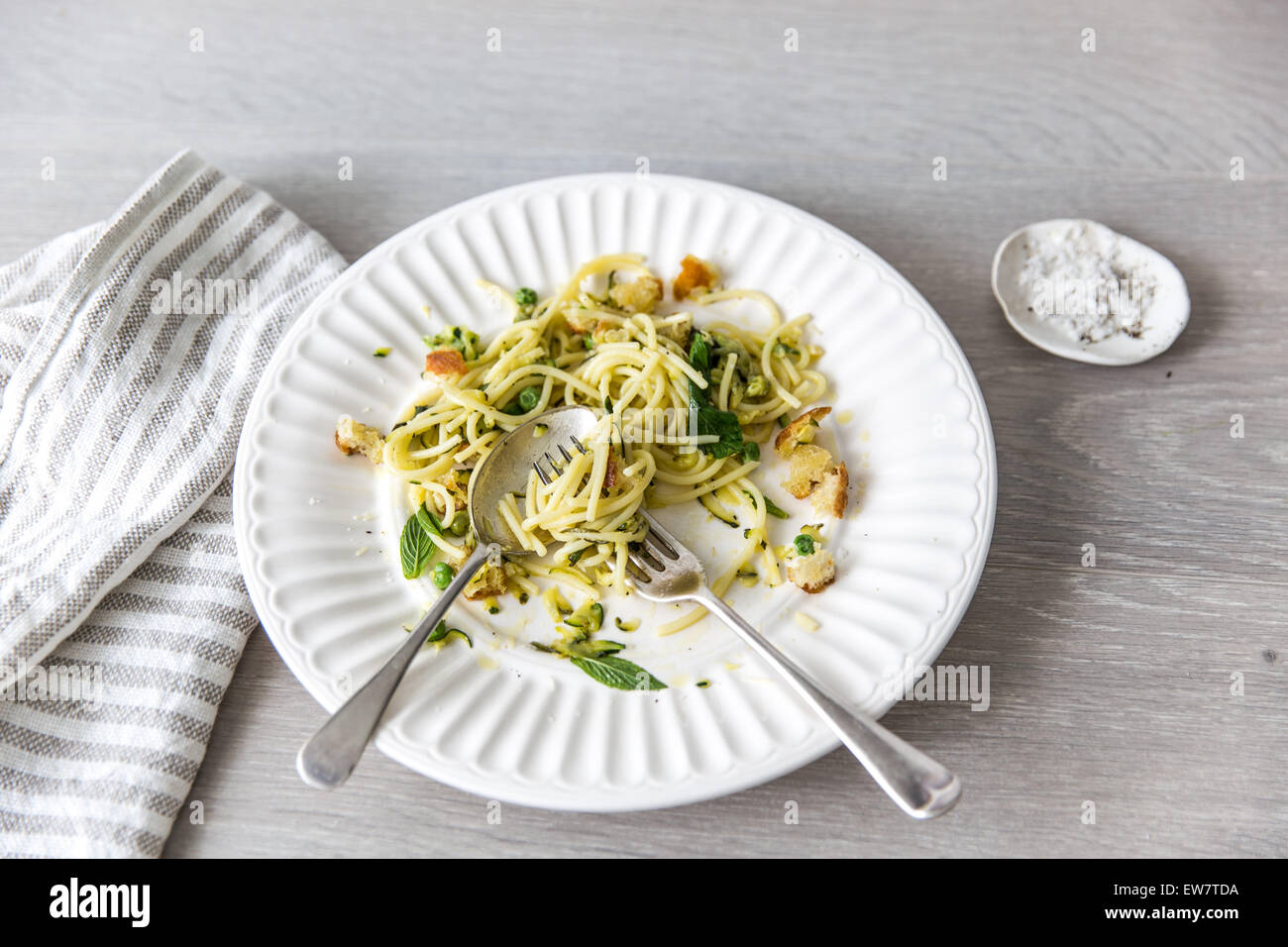 Half eaten plate of spaghetti with pea, mint, lemon, bread and parmesan ...
