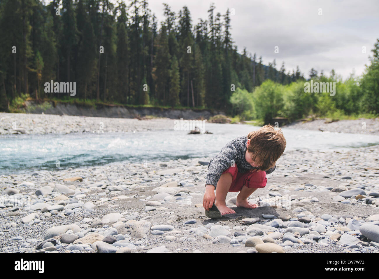 Boy looking under a rock in a river bed Stock Photo - Alamy