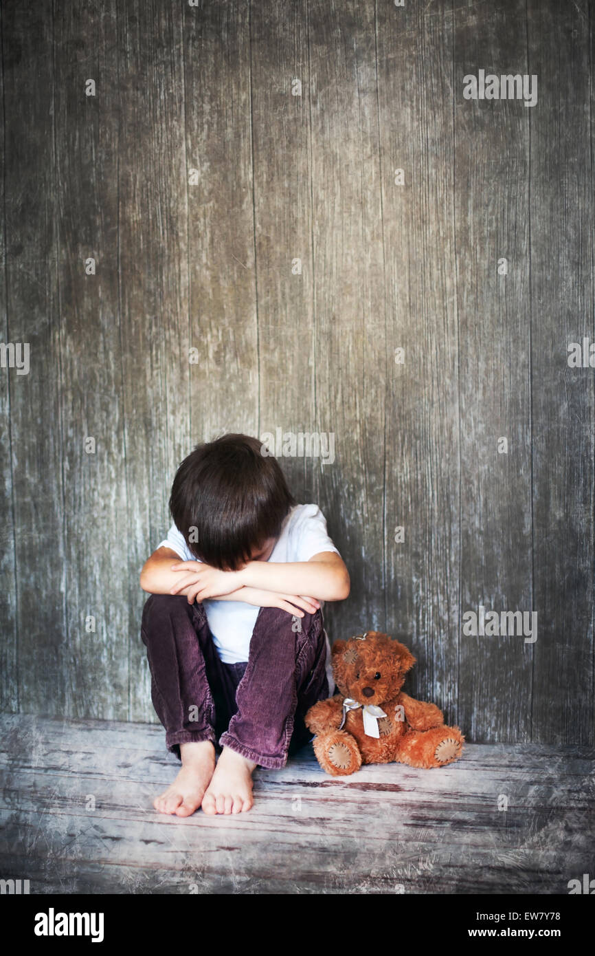 Young boy, sitting on the floor, teddy bear next to him, crying ...