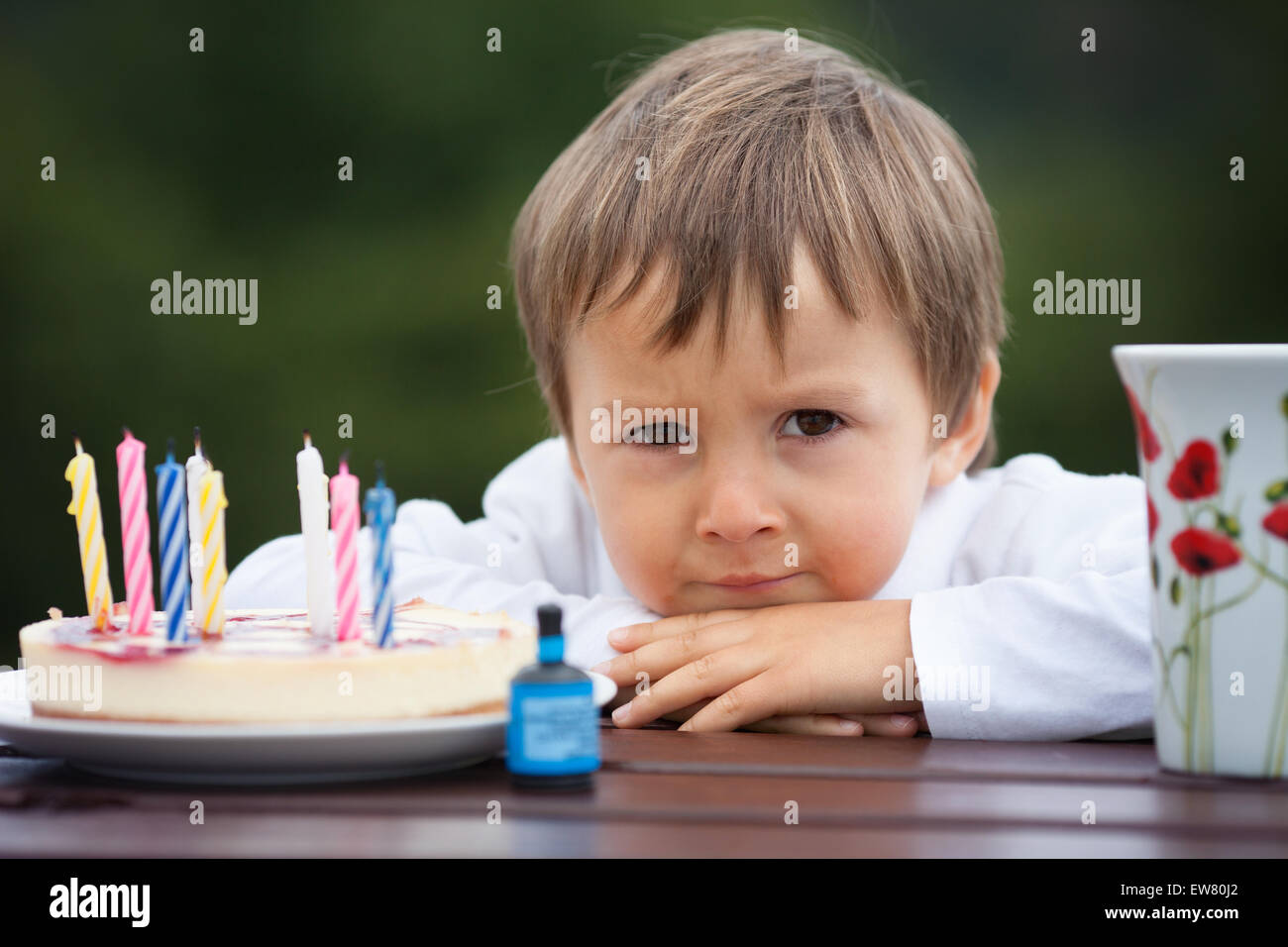 Close-up portrait of angry little boy with a cake and tea, outdoor ...