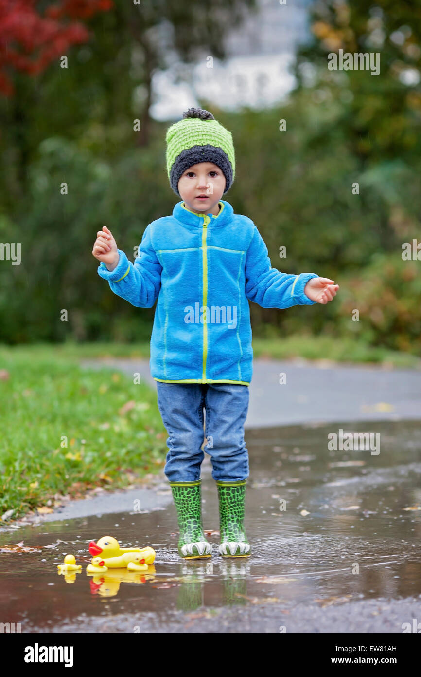 Little boy, jumping in muddy puddles in the park, rubber ducks in the ...