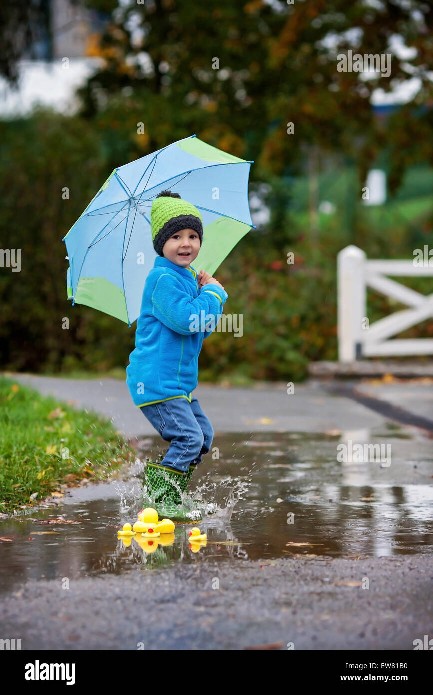 Little boy, jumping in muddy puddles in the park, rubber ducks in the ...