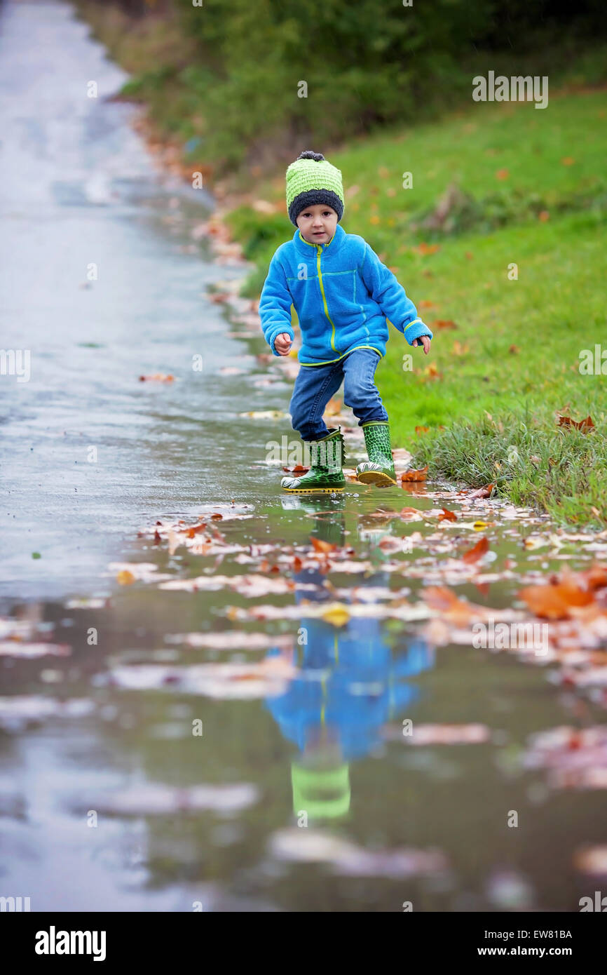 Little boy, jumping in muddy puddles in the park, rubber ducks in the ...