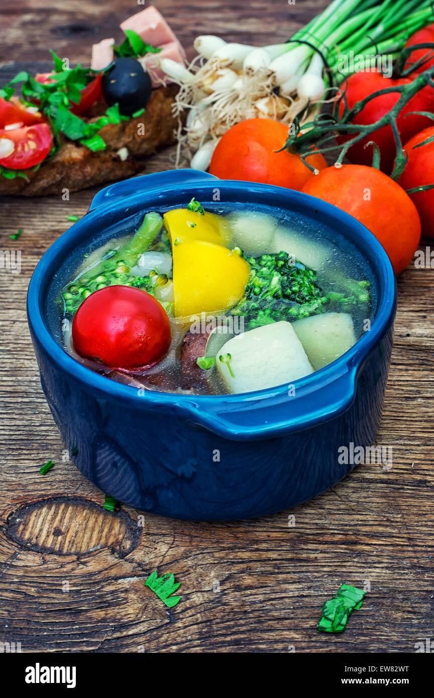 traditional soup of fresh vegetables in blue pot on wooden background ...