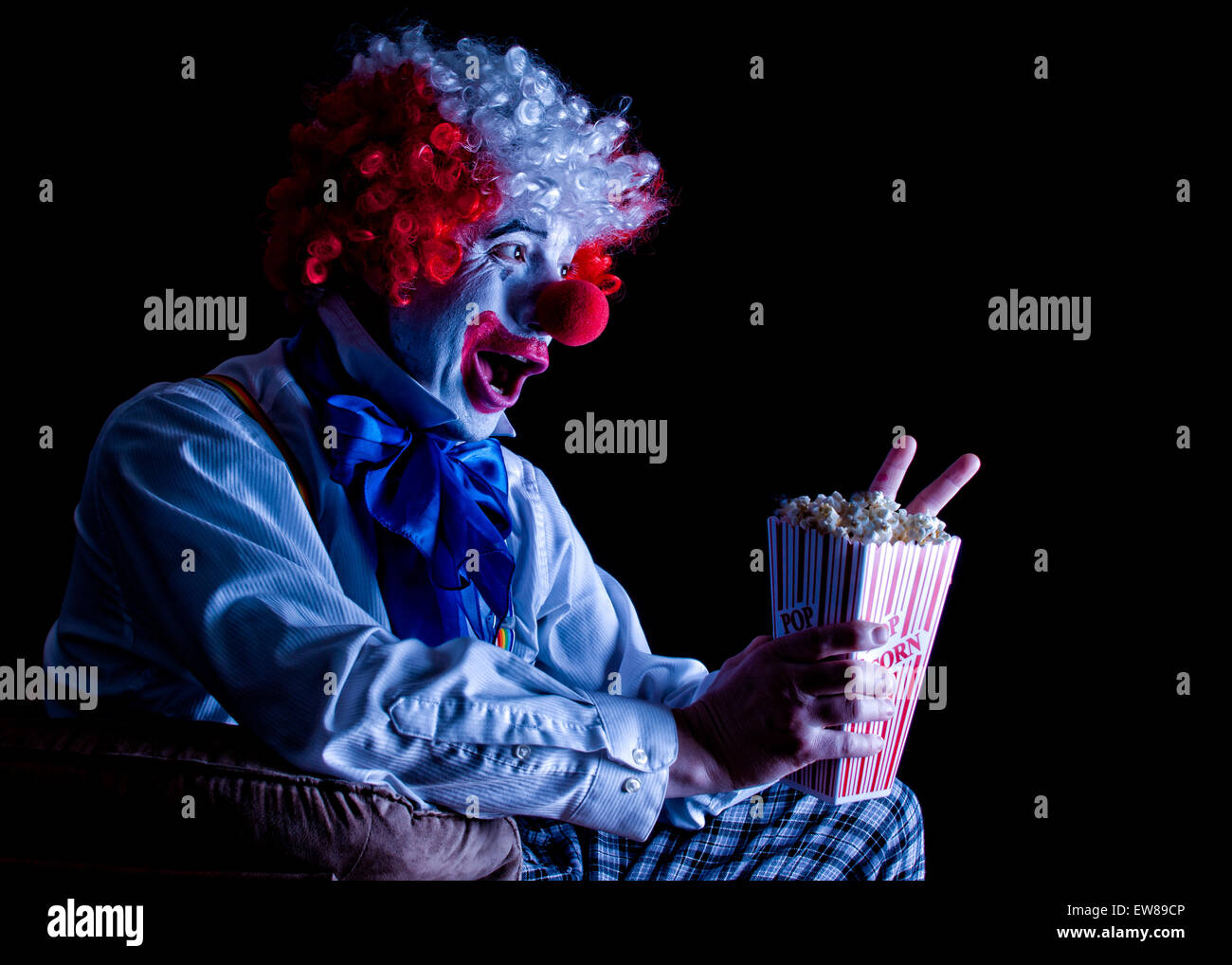 colorful clown with crazy expression eating popcorn watching a movie ...