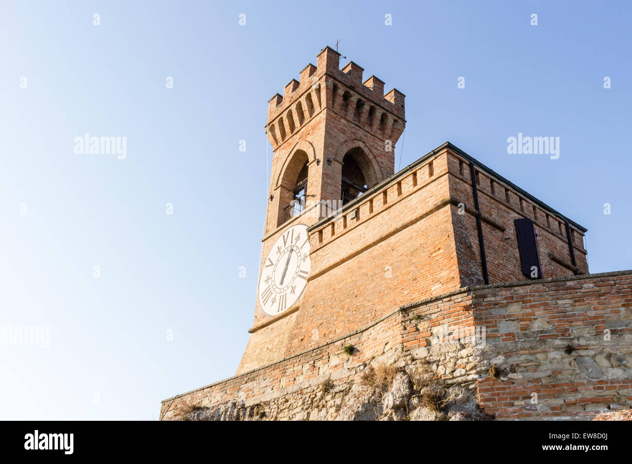 A medieval crenellated brick wall clock tower in a sunny winter day ...