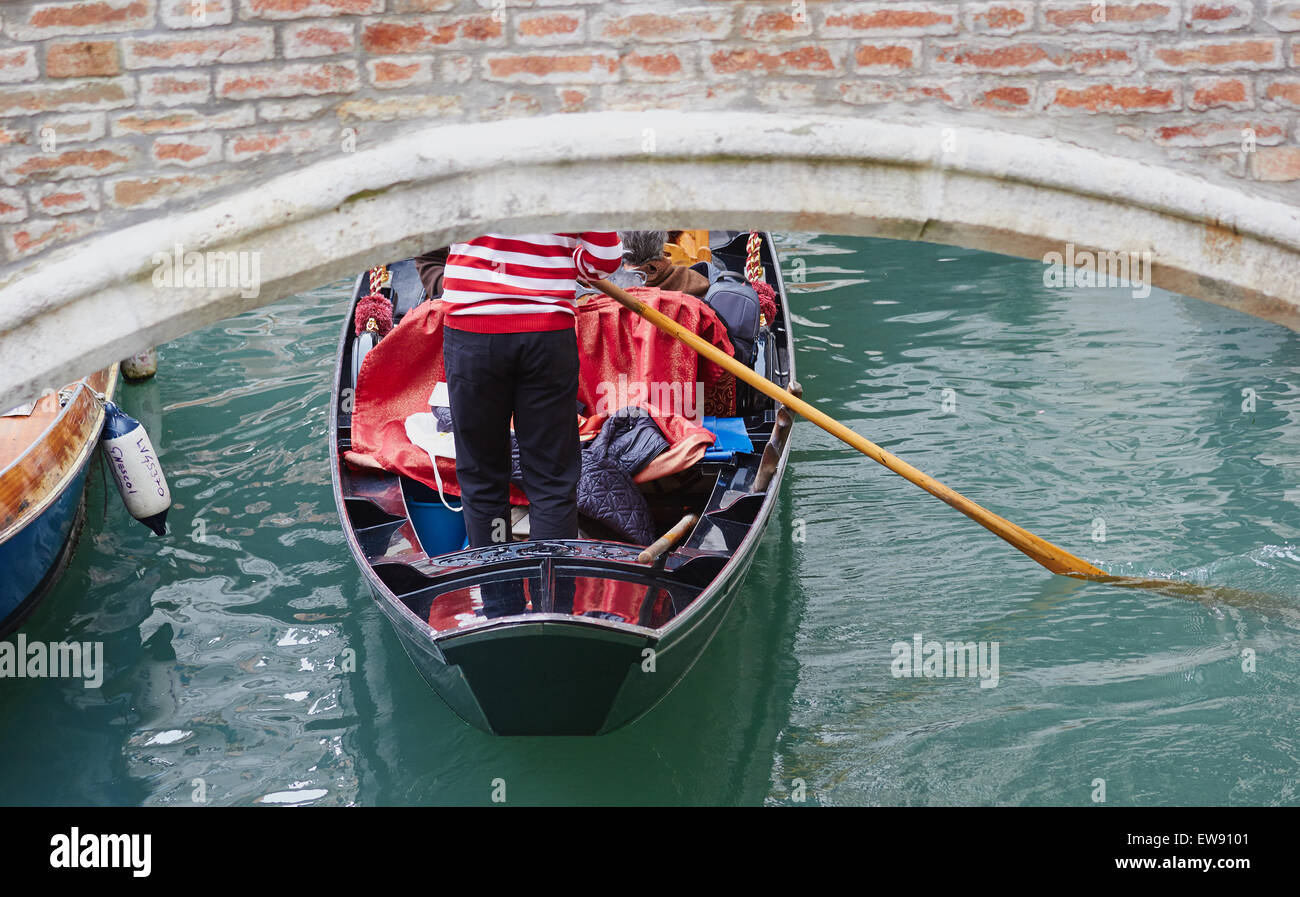 Gondolier in traditional red and white striped top rowing a gondola ...