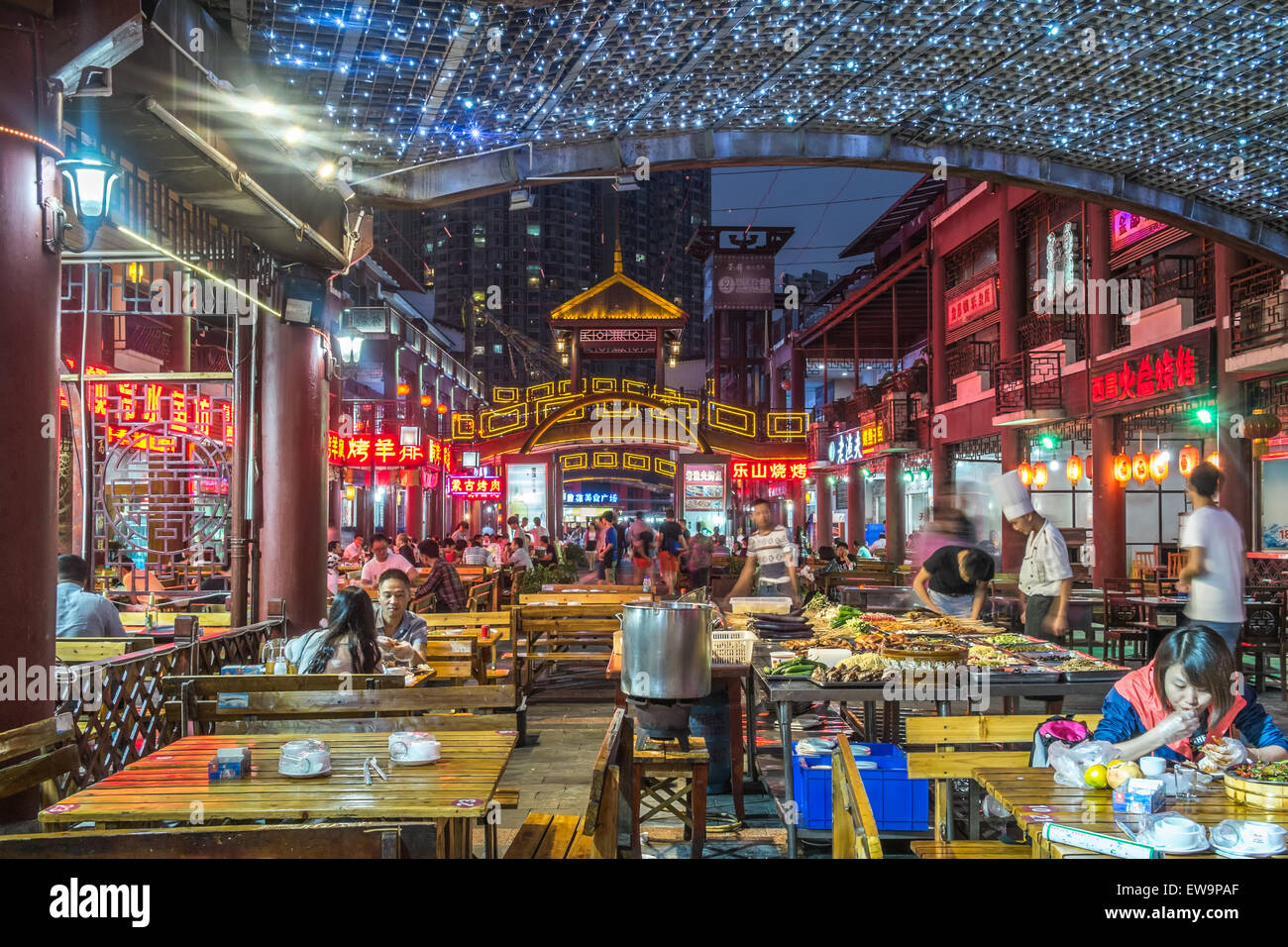 People eating outside in a neon-lit courtyard surrounded by restaurants ...