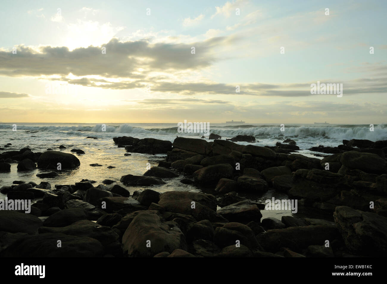 Atmospheric scene of waves breaking near rocky shoreline with early ...