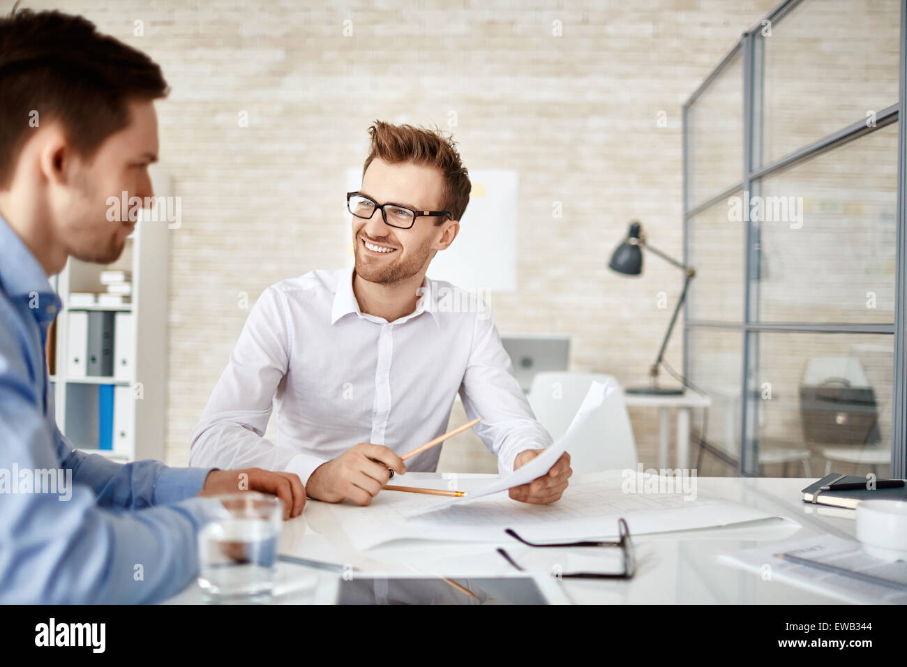 Young businessman looking at co-worker during explanation of document ...