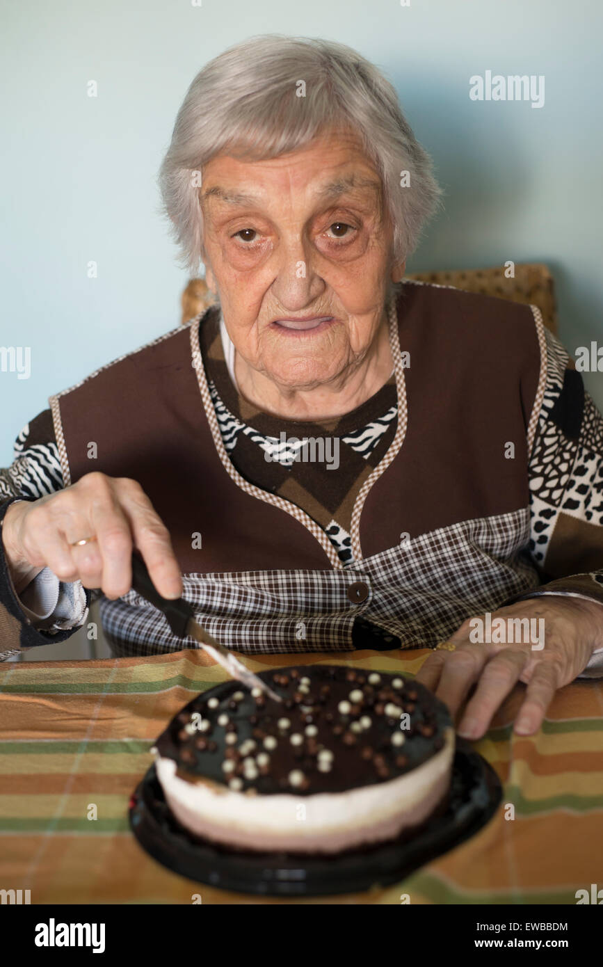 Elderly woman cutting her birthday cake at home Stock Photo - Alamy