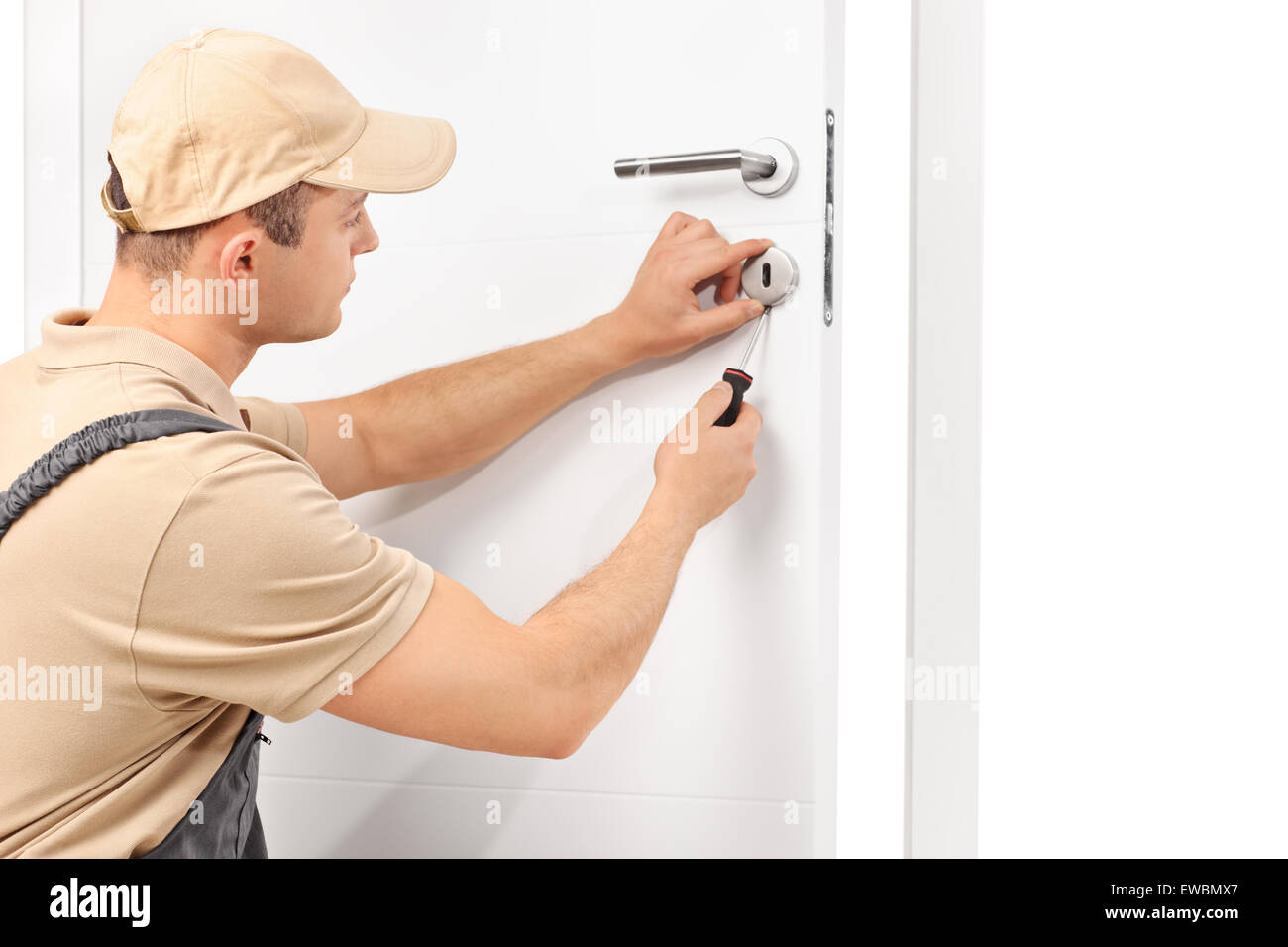 Studio shot of a young male locksmith installing a lock on a white door ...