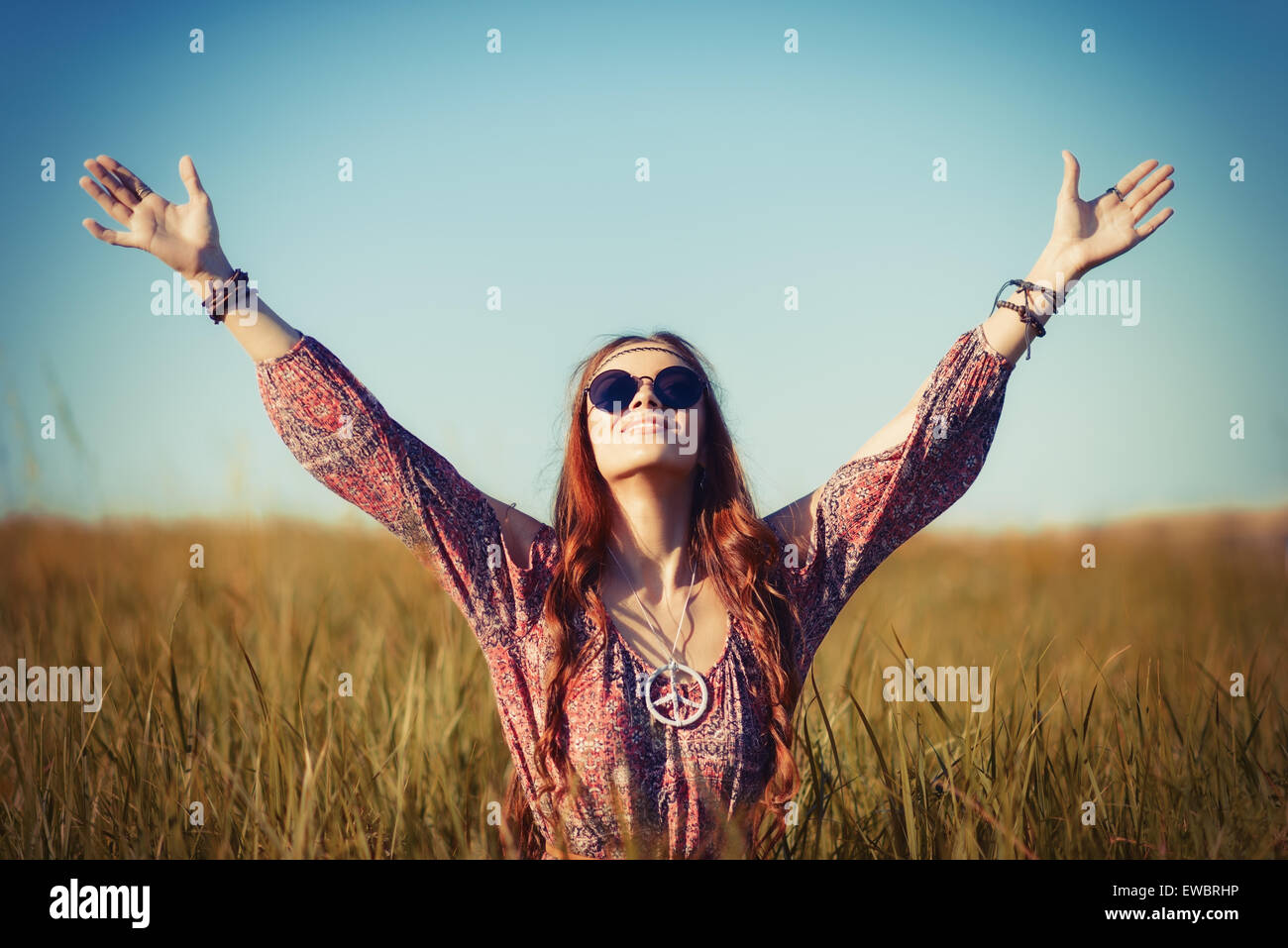 Beautiful young hippie woman sitting in the field and praying to God ...