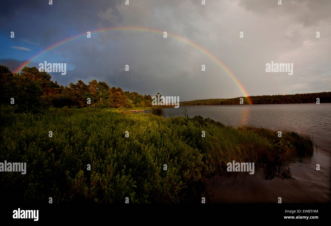 A rainbow forms over a lake after a summer rain Stock Photo - Alamy