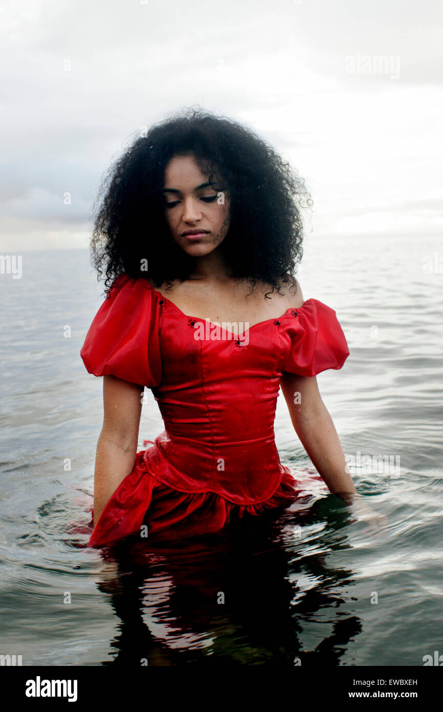 A young woman poses in the Pacific Ocean in a red dress near the town ...
