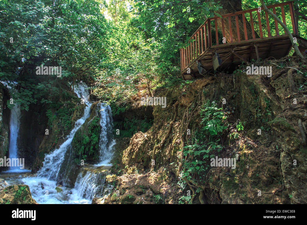 Bottom view of flowing waterfall and observation terrace among trees ...