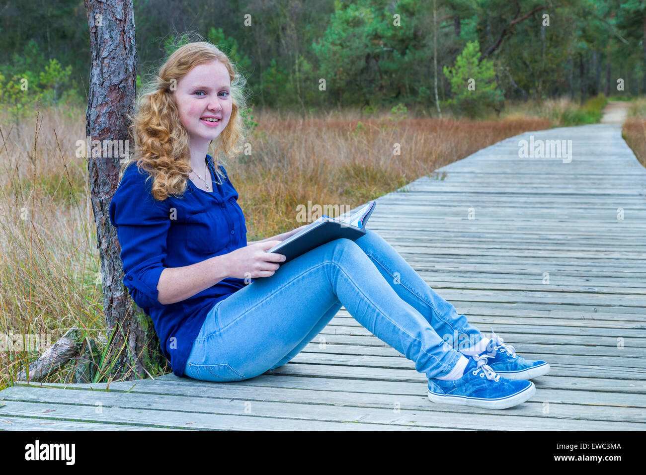 European teenage girl reading book on wooden path in forest Stock Photo ...