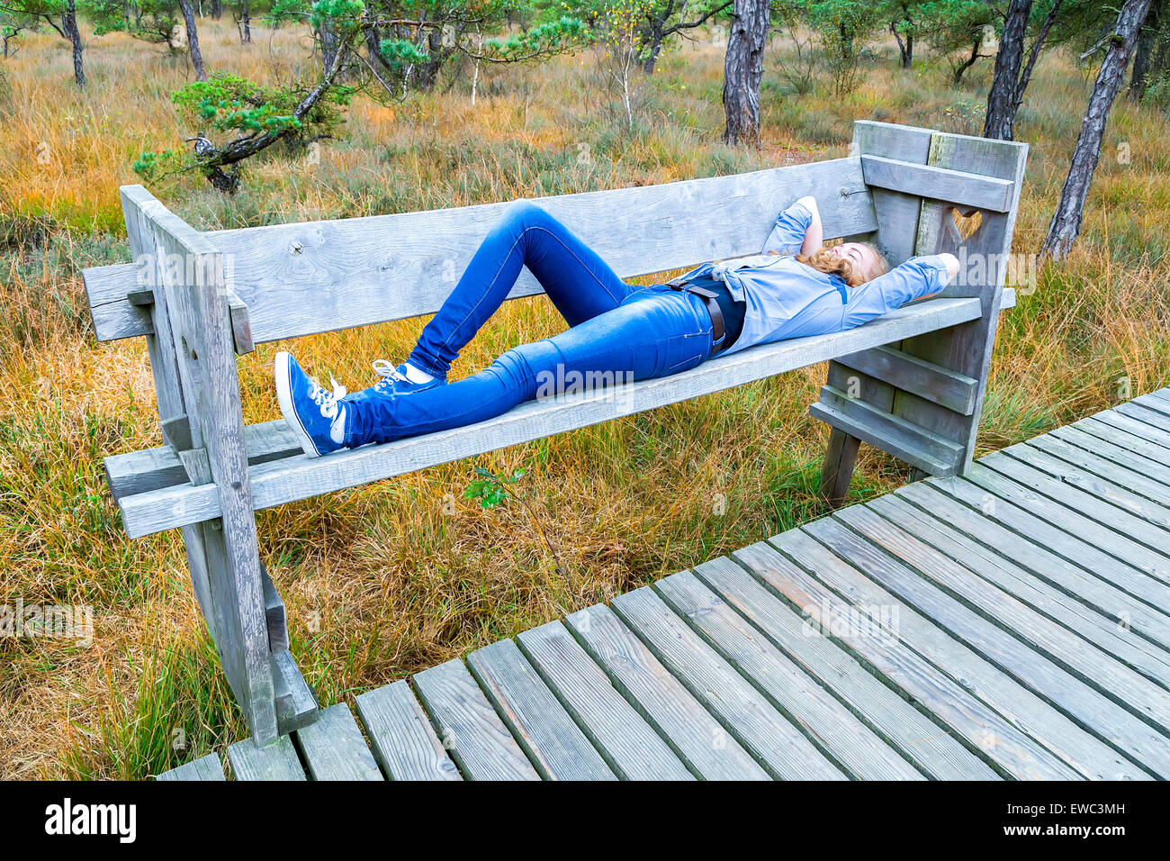 Teenage girl lying on wooden bench near path in forest Stock Photo - Alamy