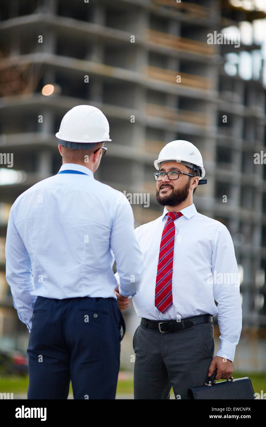 Successful architects greeting one another near building structure ...