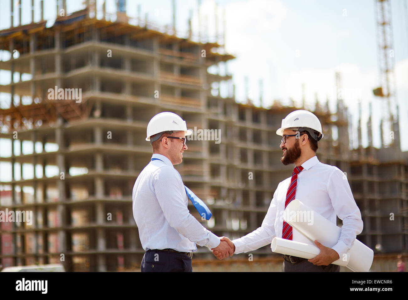 Happy modern architects handshaking on background of building structure ...