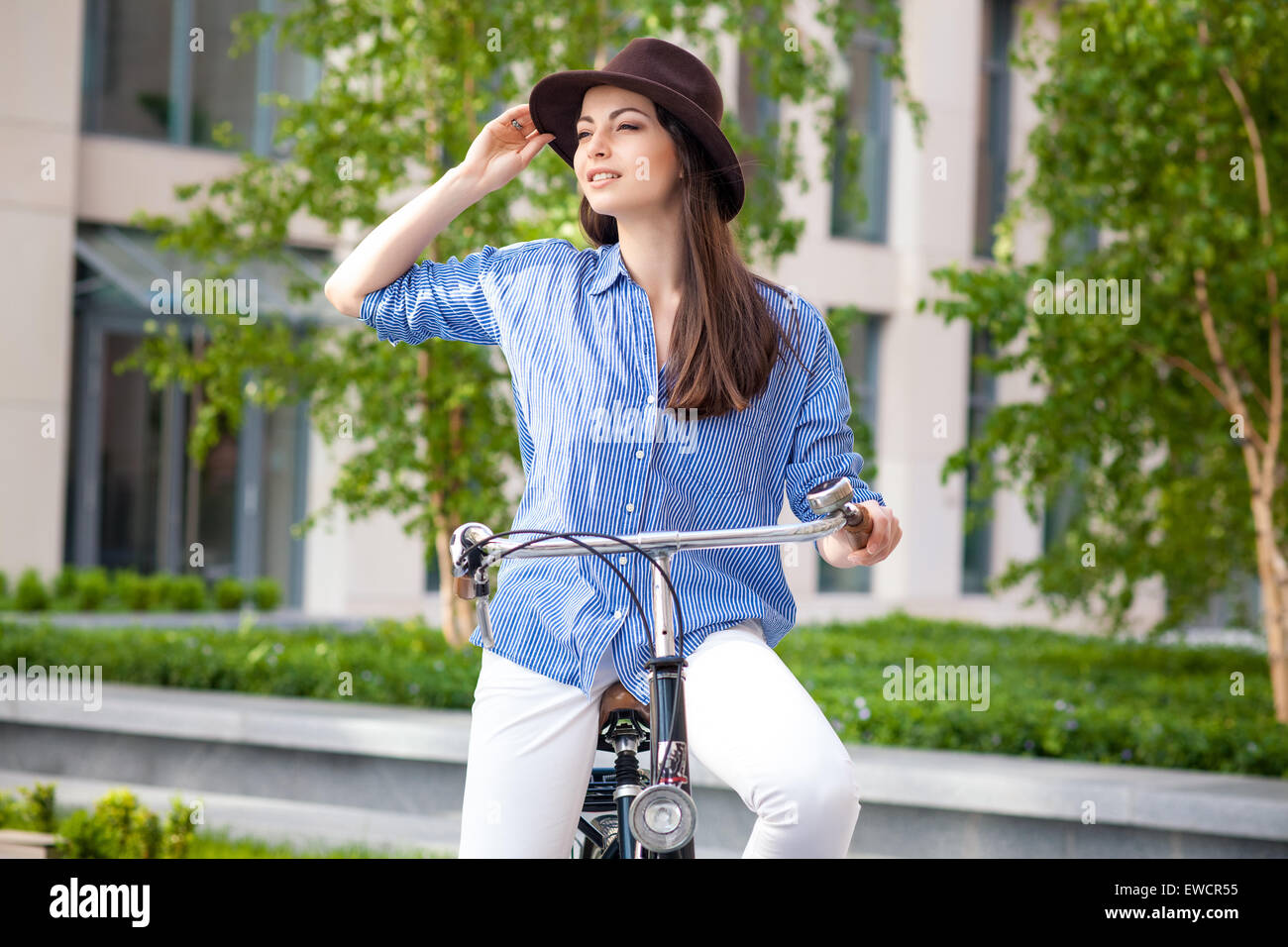 Pretty smiling girl in hat and blue dress riding a bicycle at green ...